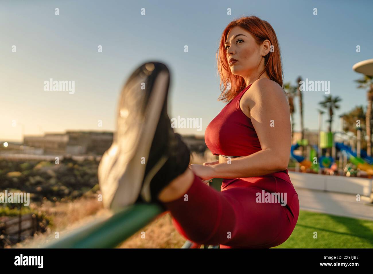 Plus-size woman stretching her leg on a railing during outdoor workout ...