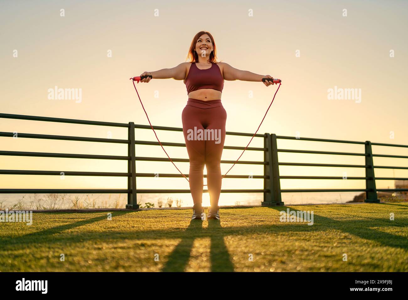 Plus-size woman jump roping during an outdoor workout at sunset ...