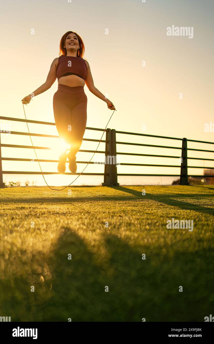 Plus-size woman jump roping during an outdoor workout at sunset ...