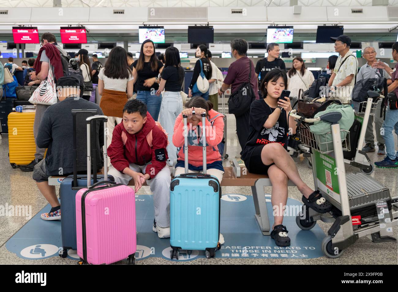 Passengers wait in line and sit on a bench at the Emirates airline ...