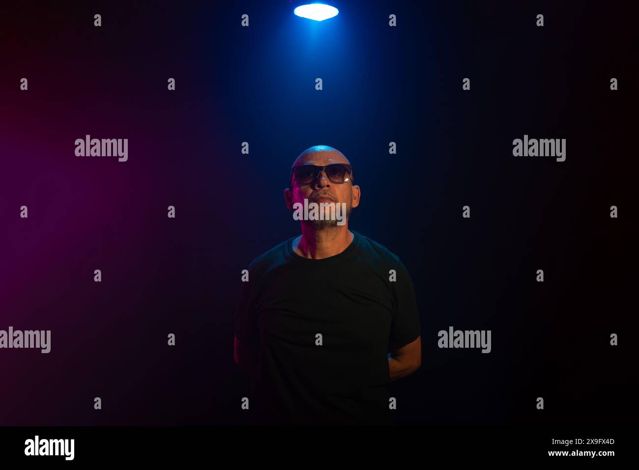 Bald man with a beard wearing sunglasses looking forward. Light above ...