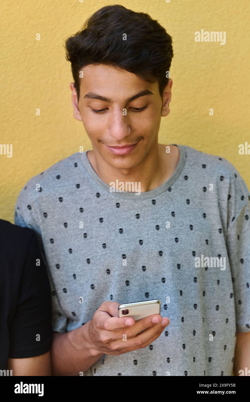 Middle Eastern Teenager Using Mobile Phone While Leaning Against Yellow ...