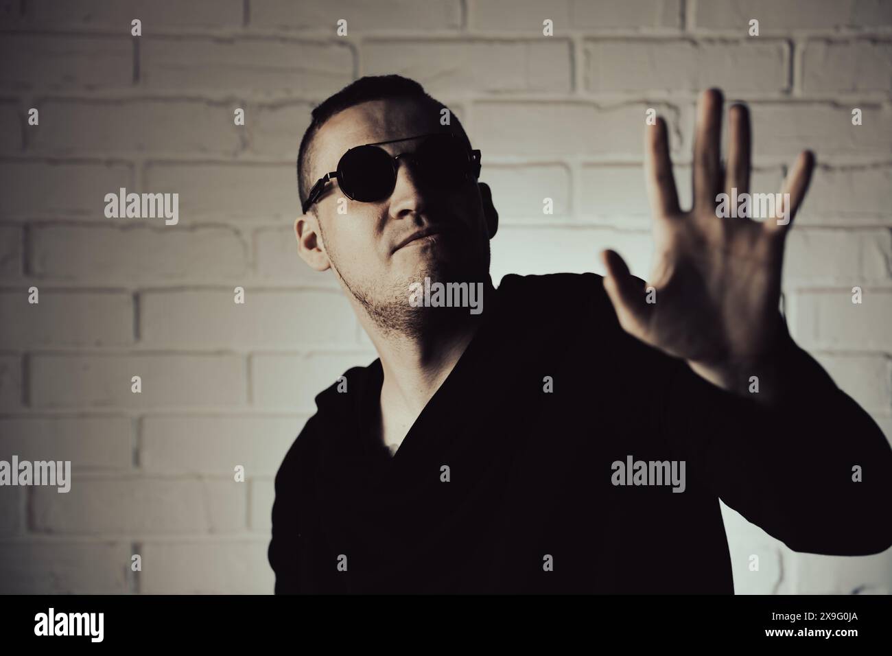 Man Posing Dramatically in Sunglasses Against White Brick Wall at Night ...