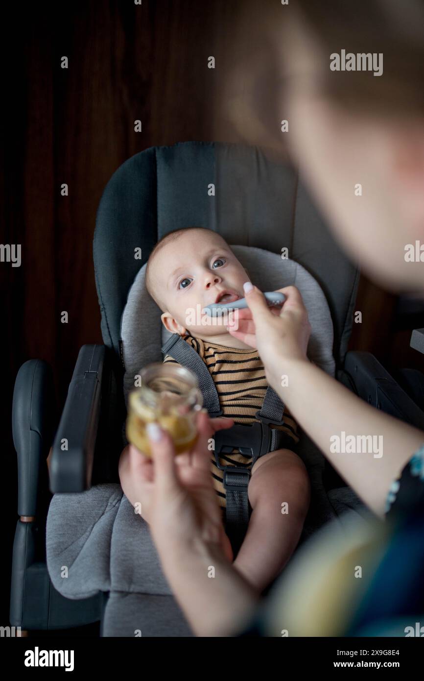 Mother feeding her son in a high chair. Baby's first complementary food ...