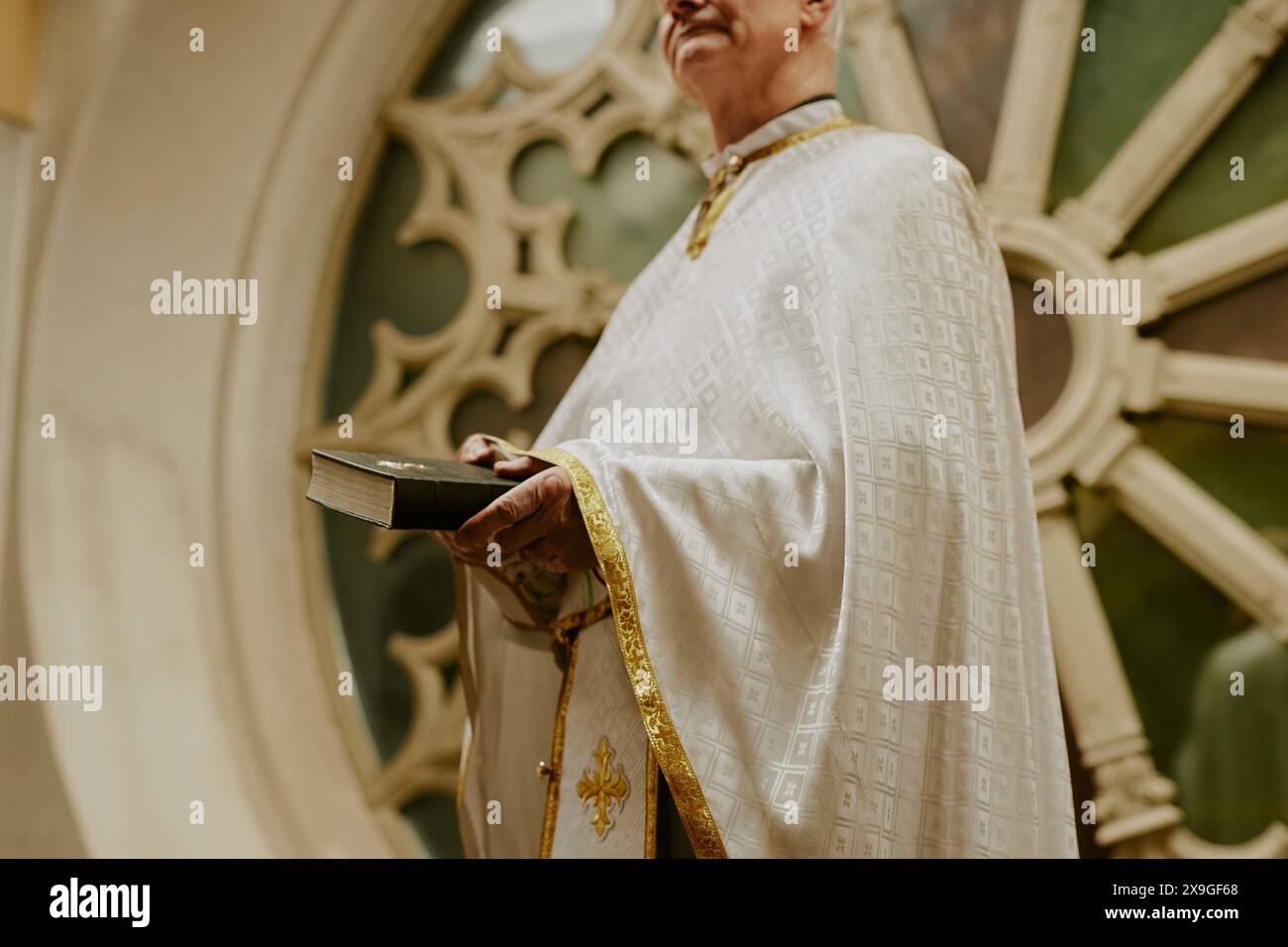 Low angle view of senior Catholic priest wearing vestment holding Bible ...