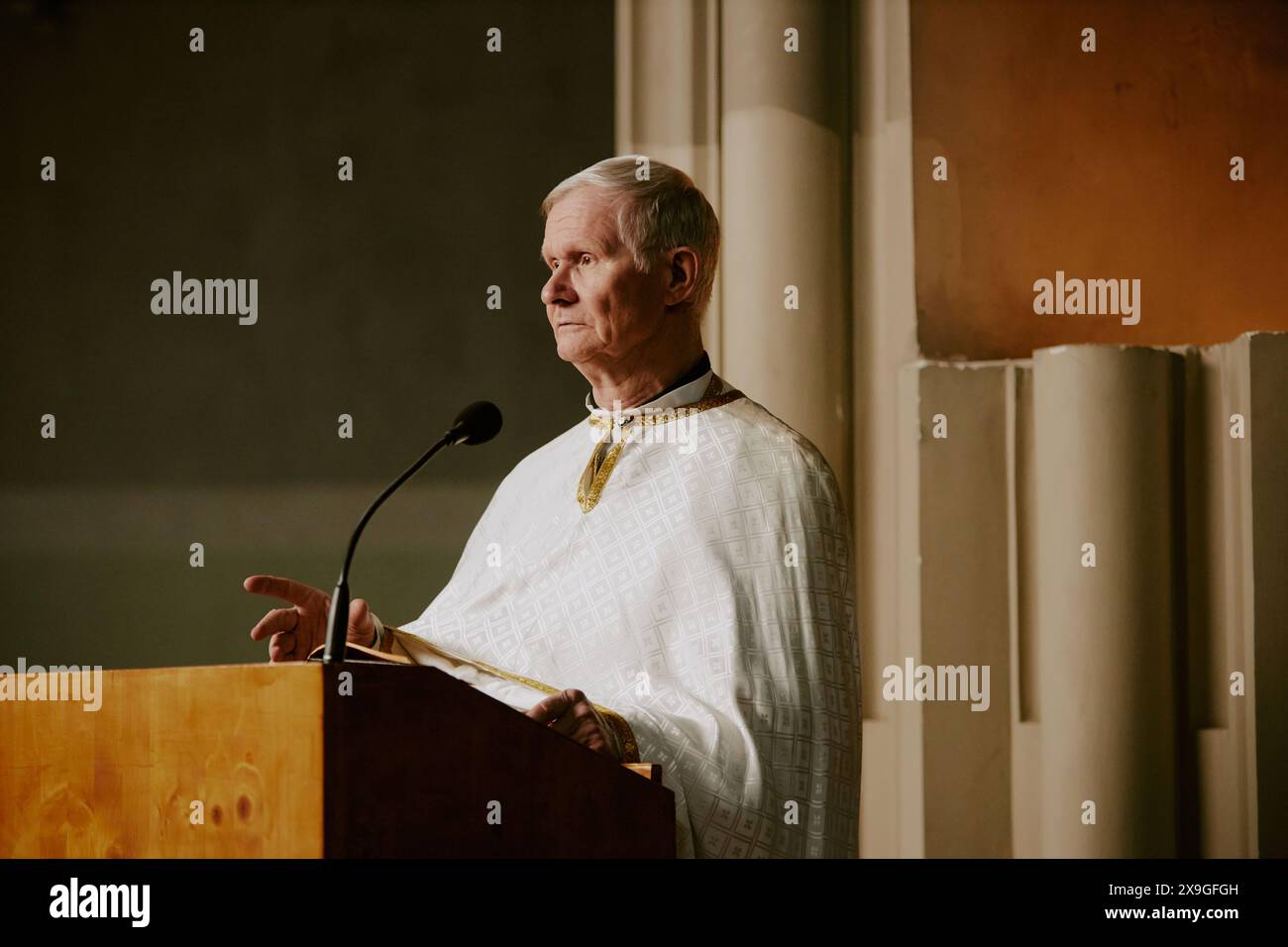 Medium shot of elderly Caucasian Catholic priest standing at lectern ...