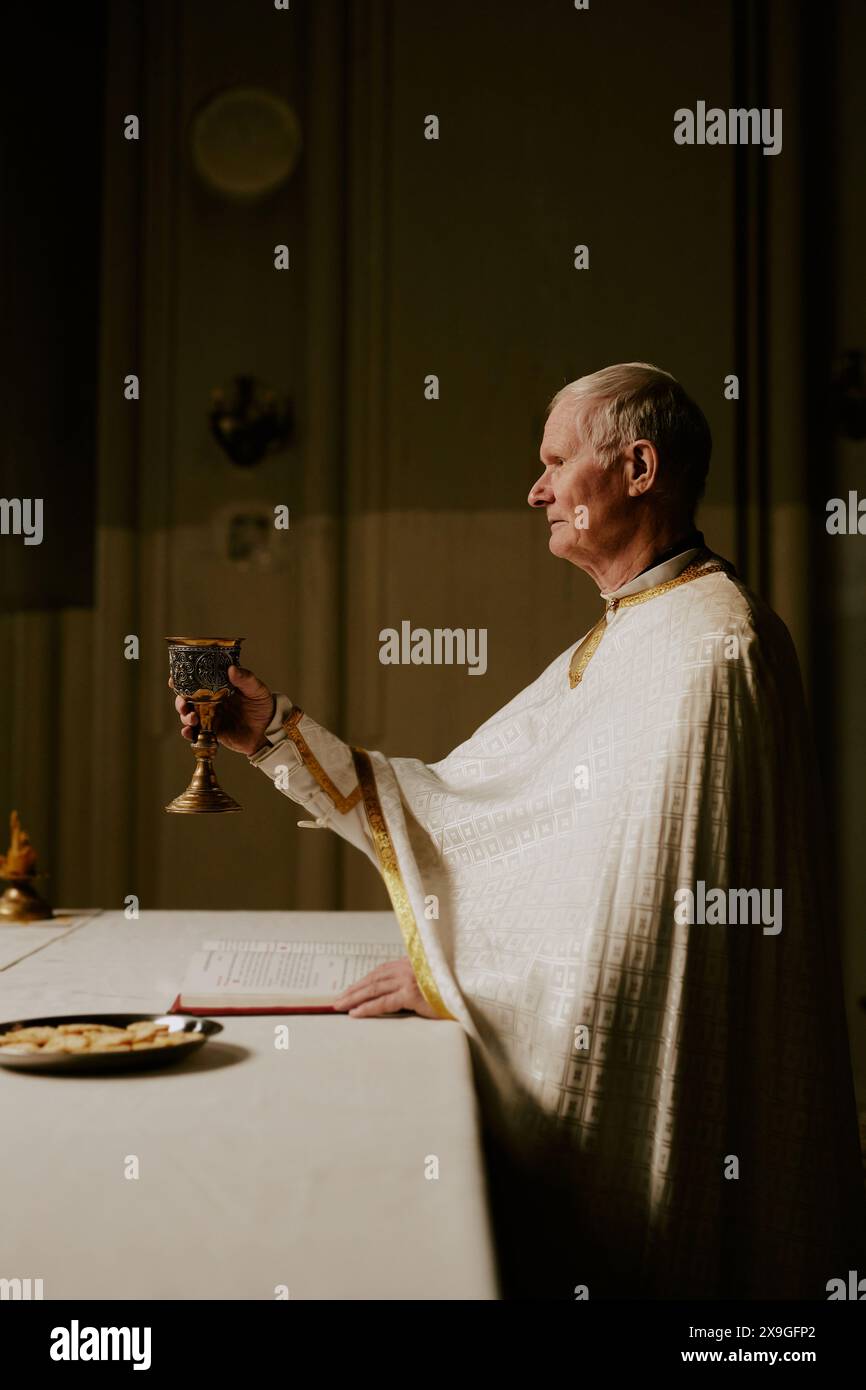 Vertical side view shot of senior Caucasian Catholic priest holding cup ...