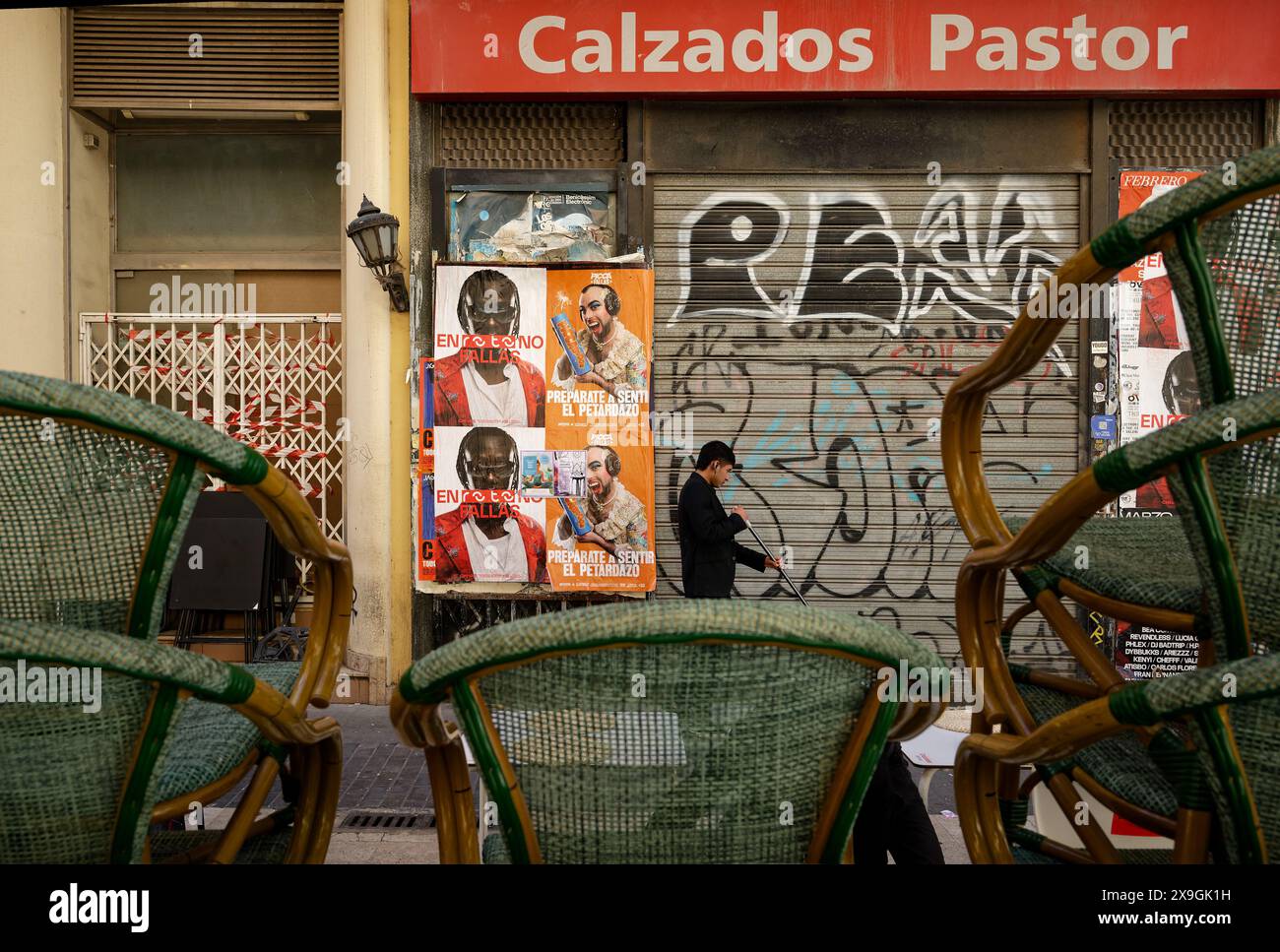Man sweeps in front of a closed storefront with graffiti and festival ...