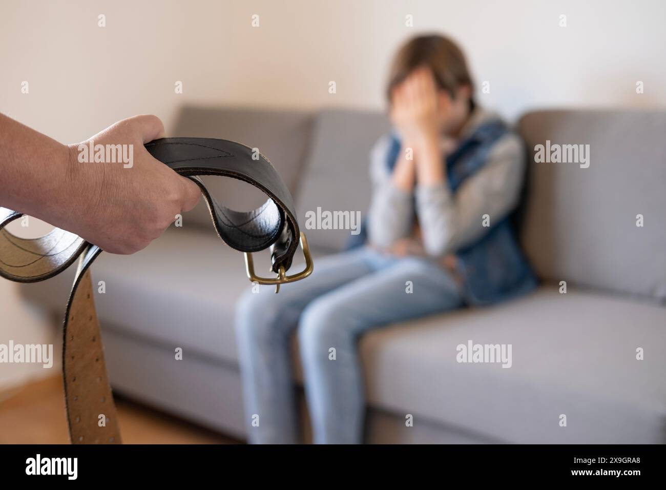 woman with leather belt in hand confronts teenage child on couch ...