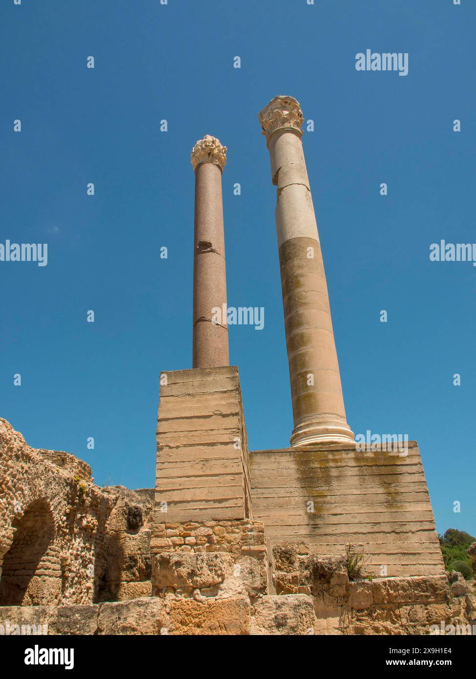 Two tall ancient columns rise into the blue sky, surrounded by ancient ...