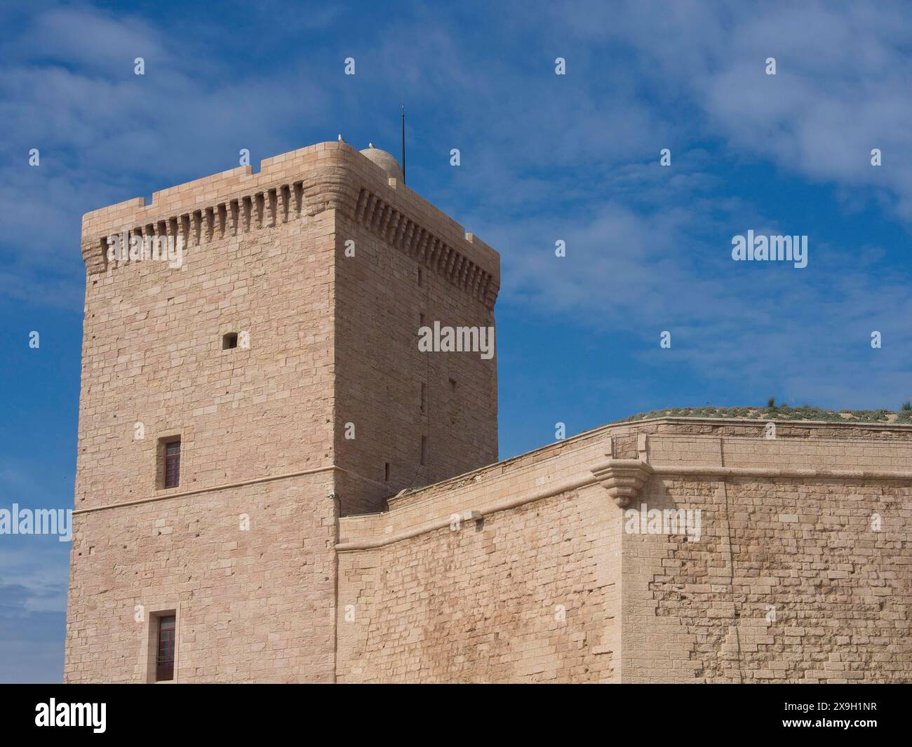 Historic stone tower of a fortress under a slightly cloudy blue sky ...