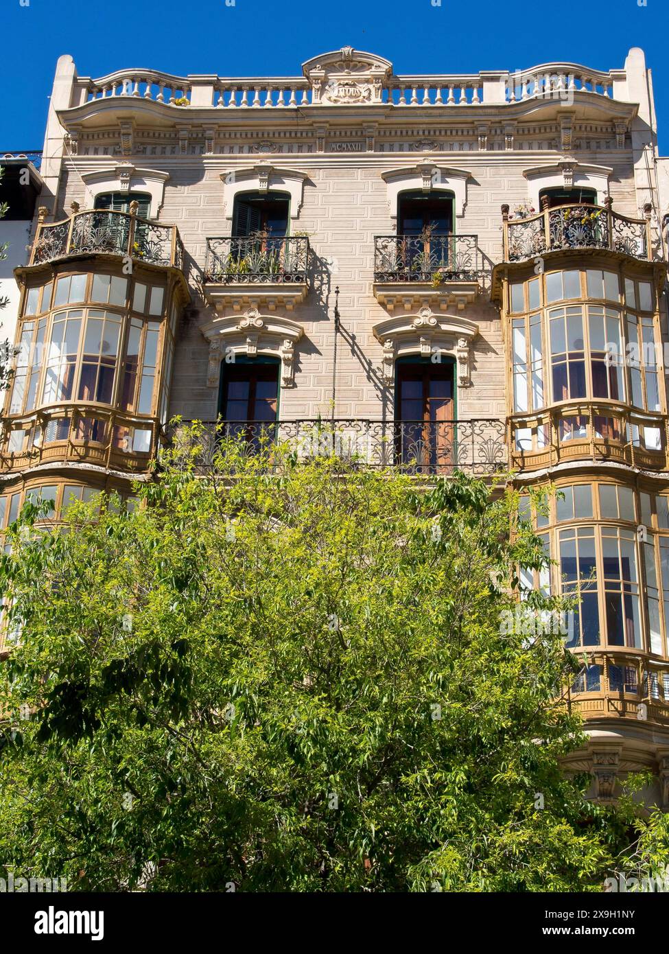 Close-up of a historic facade with numerous balconies and green trees ...