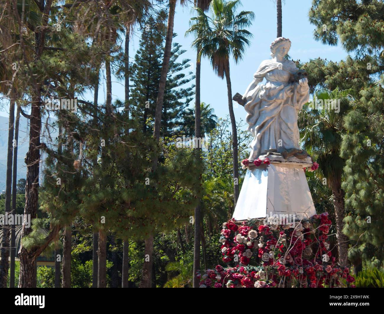 White statue in a park surrounded by palm trees and other trees under a ...