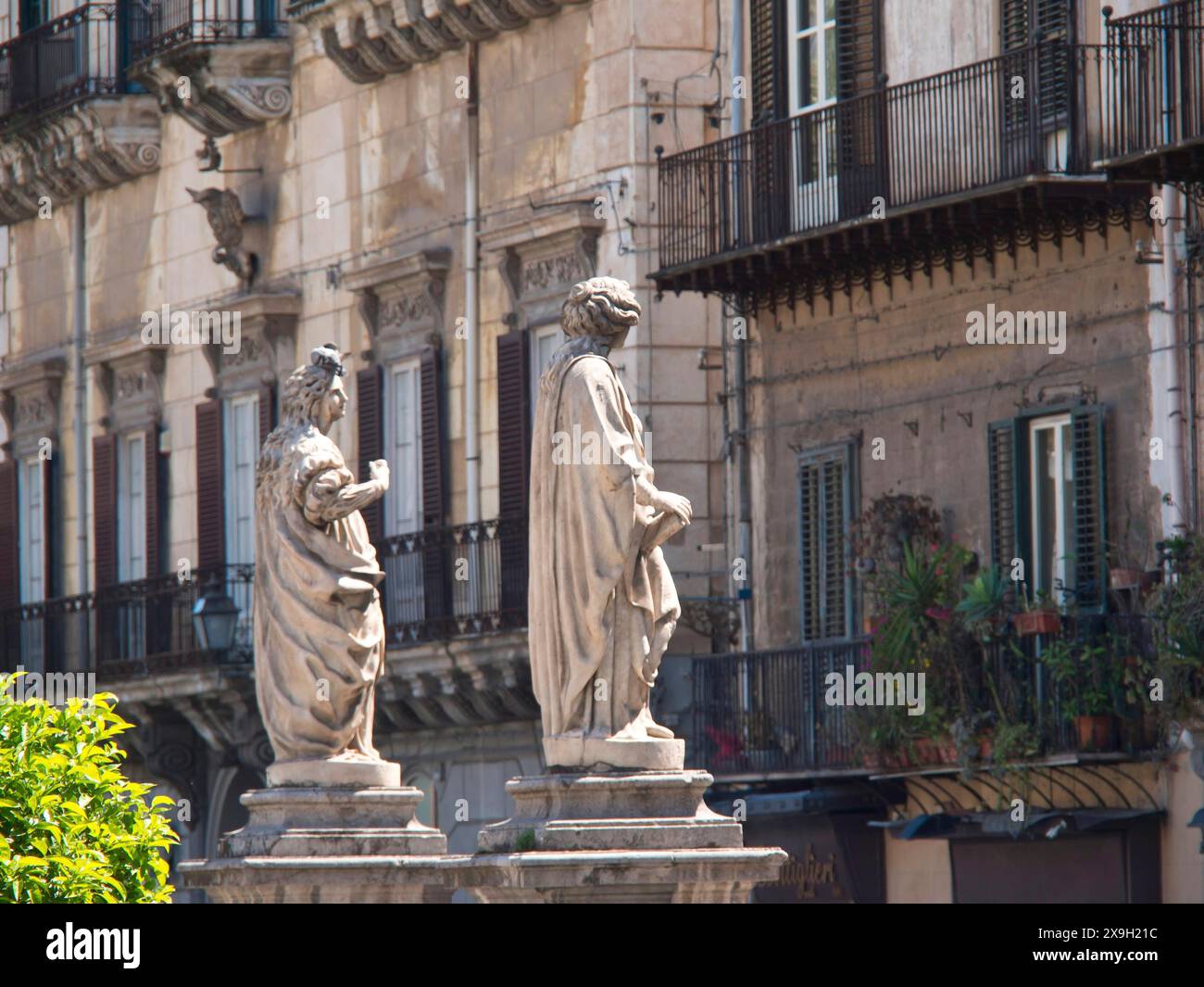 Two statues in front of old buildings with balconies, an antique look ...