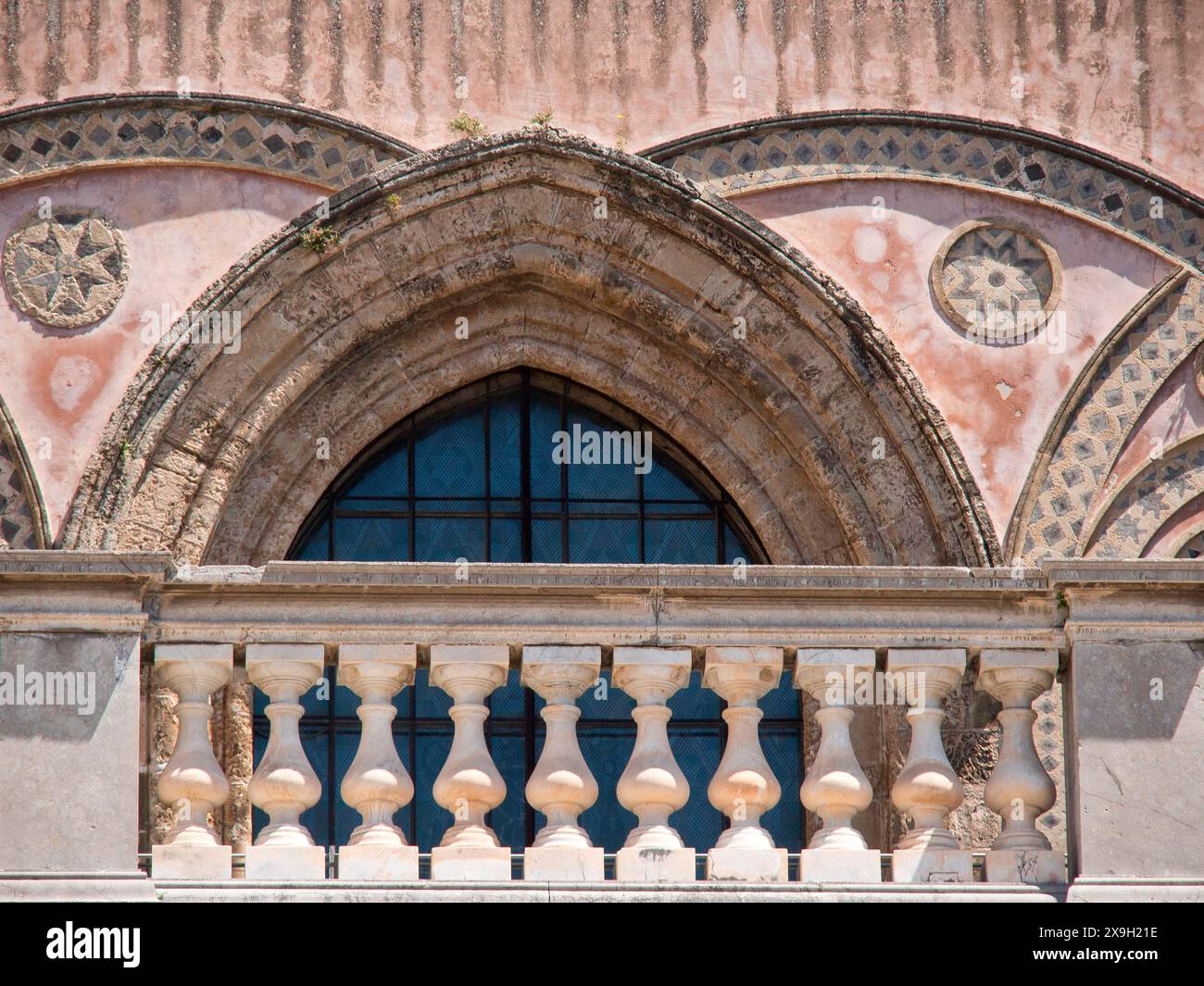 An arched window with ornate stone ornaments on a historic pink ...