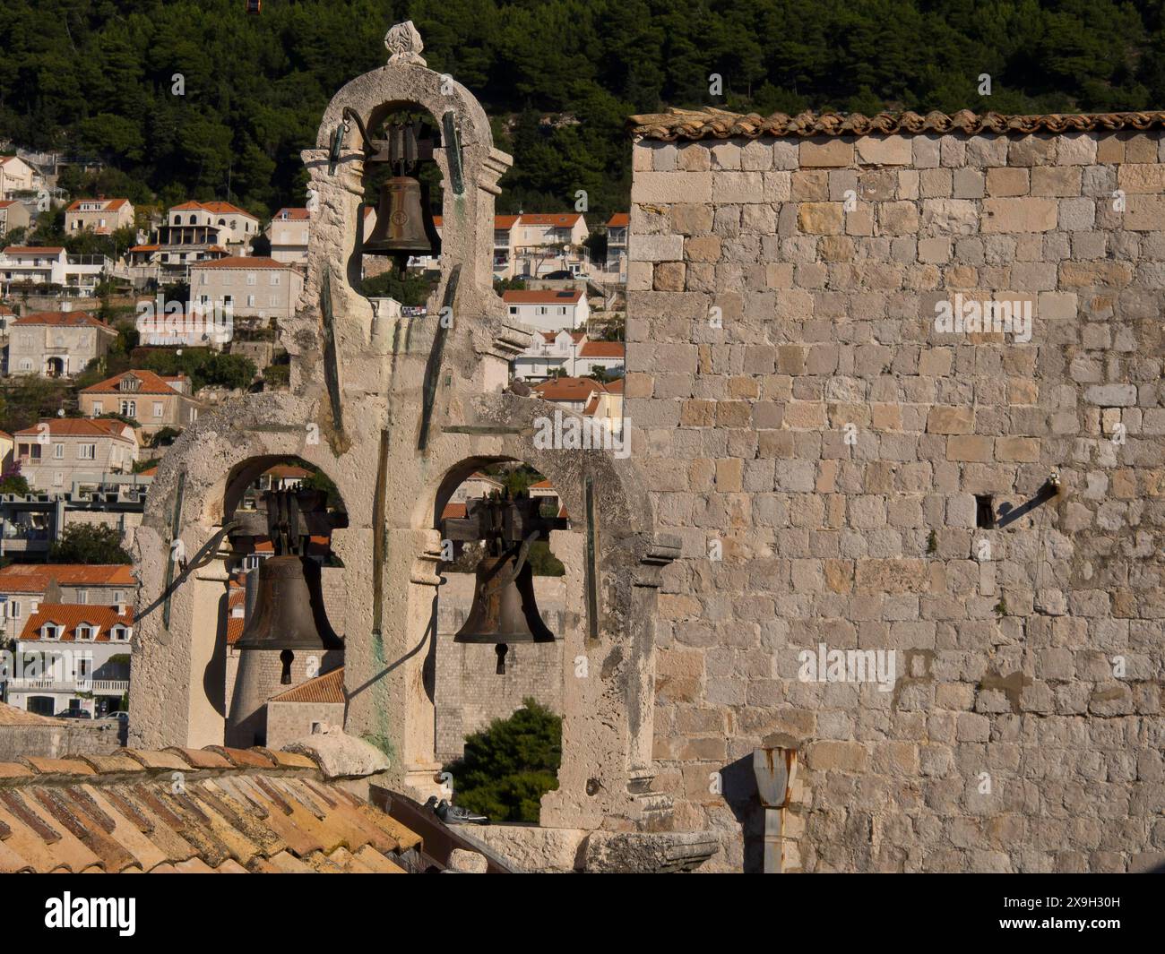 Historic bell tower with three bells in front of a wall, surrounded by ...
