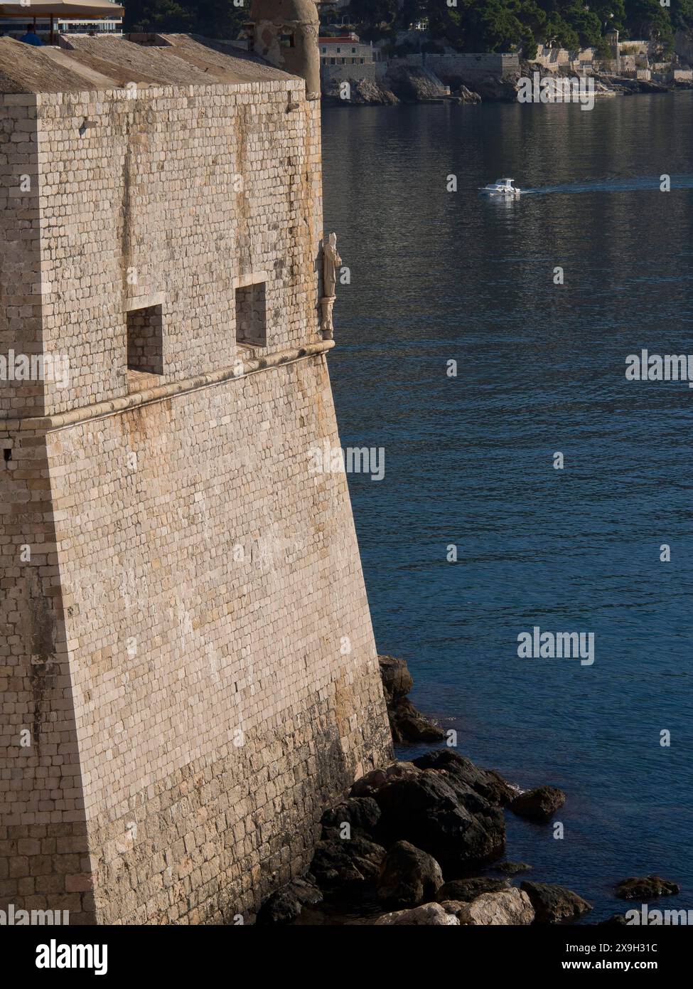 Massive stone walls of a fortress tower over the calm sea with a small ...