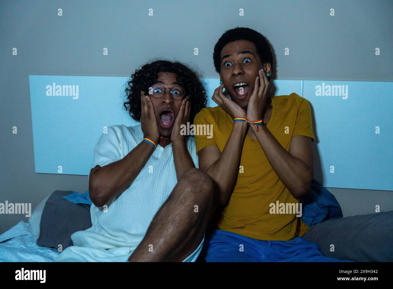 Scared gay couple with hands on face and open mouth watching horror ...