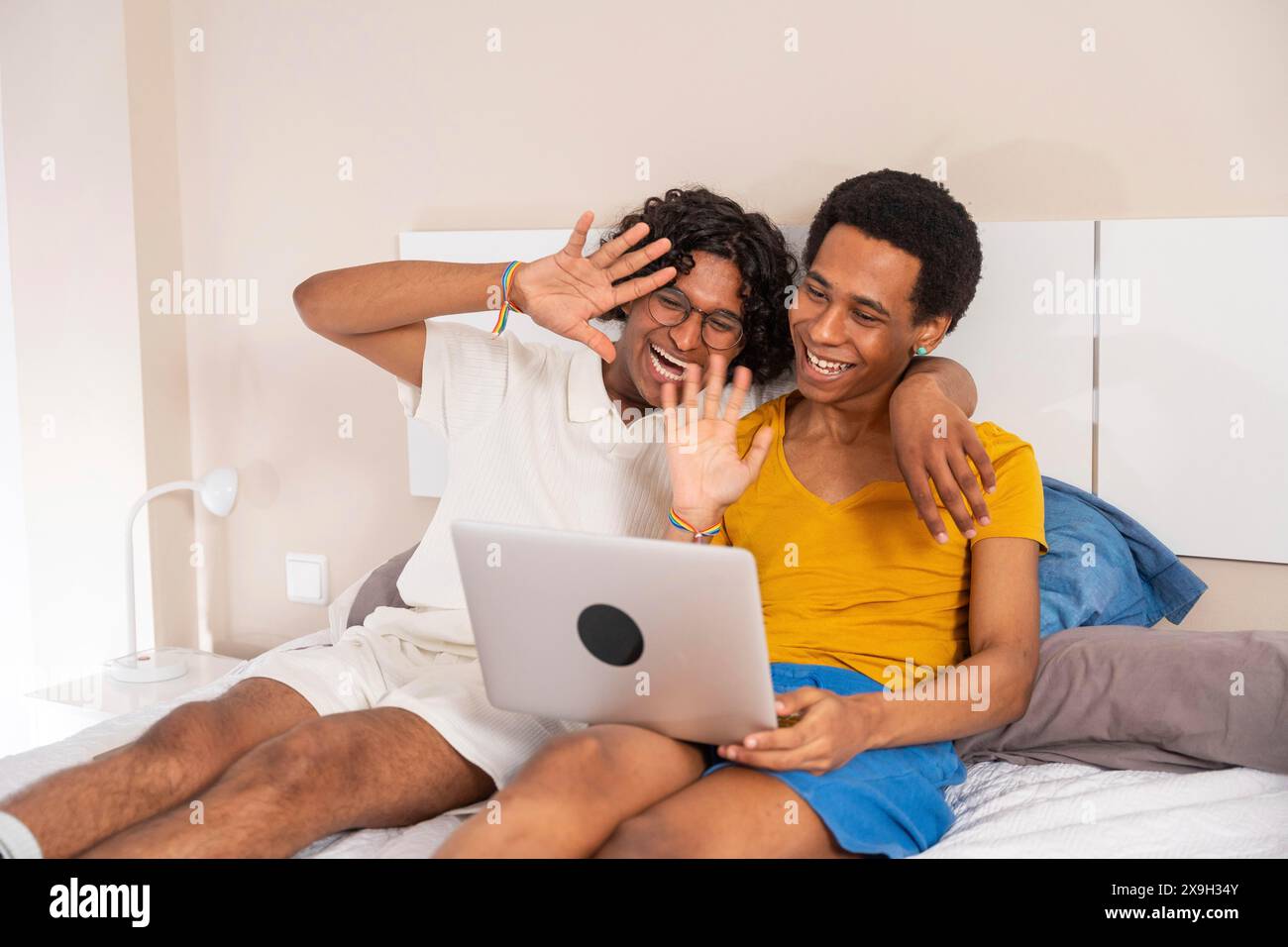 Gay couple waving during a video call with laptop lying on bed Stock ...