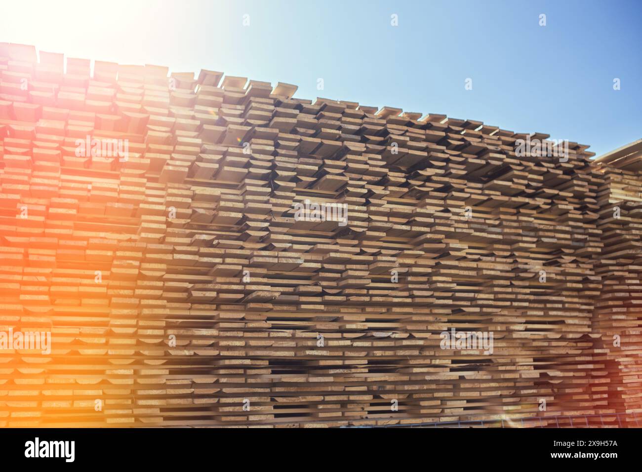 A large stack of lumber boards is neatly stacked at a lumber yard. The ...