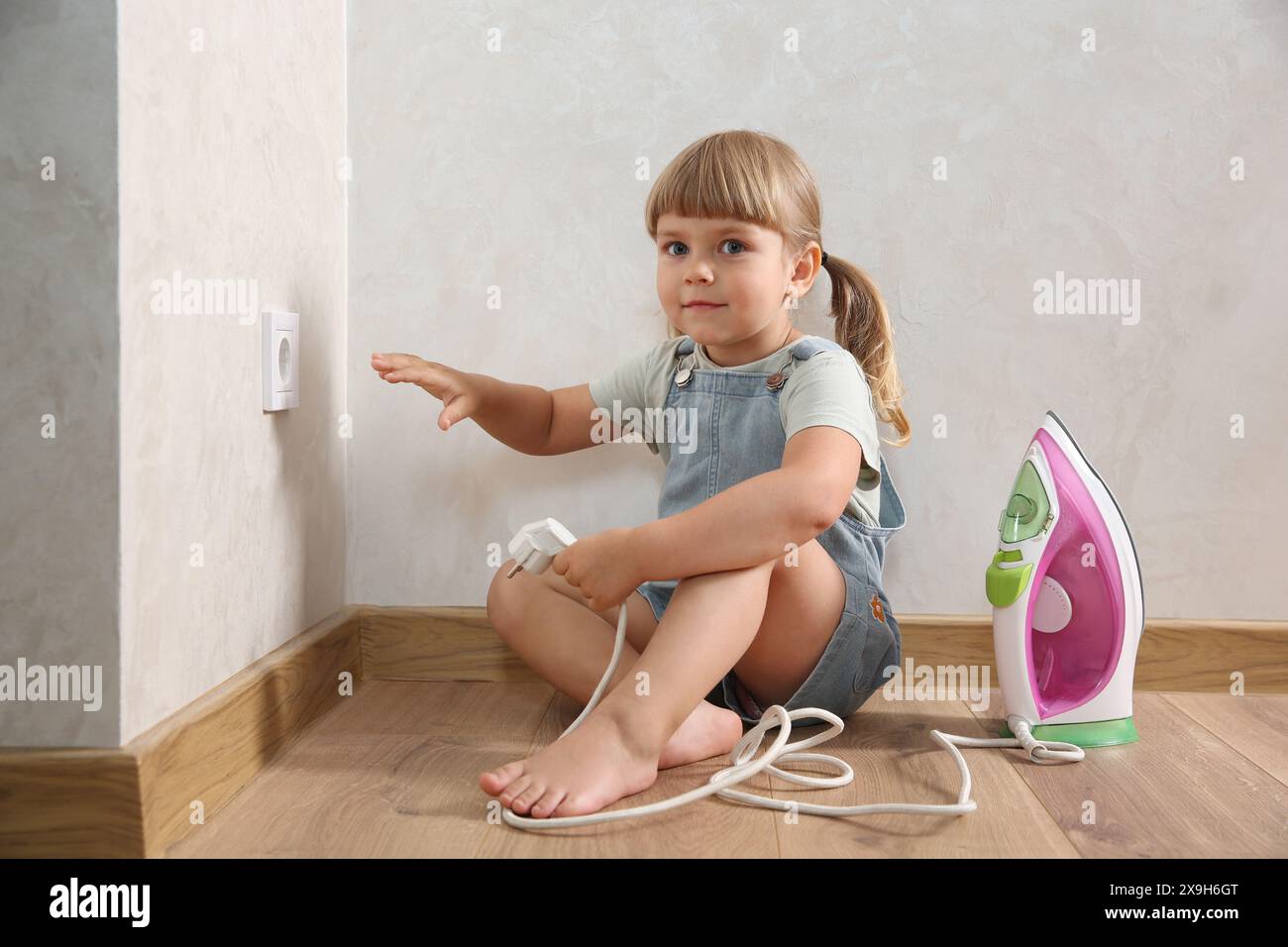 Little child playing with electrical socket and iron plug at home ...