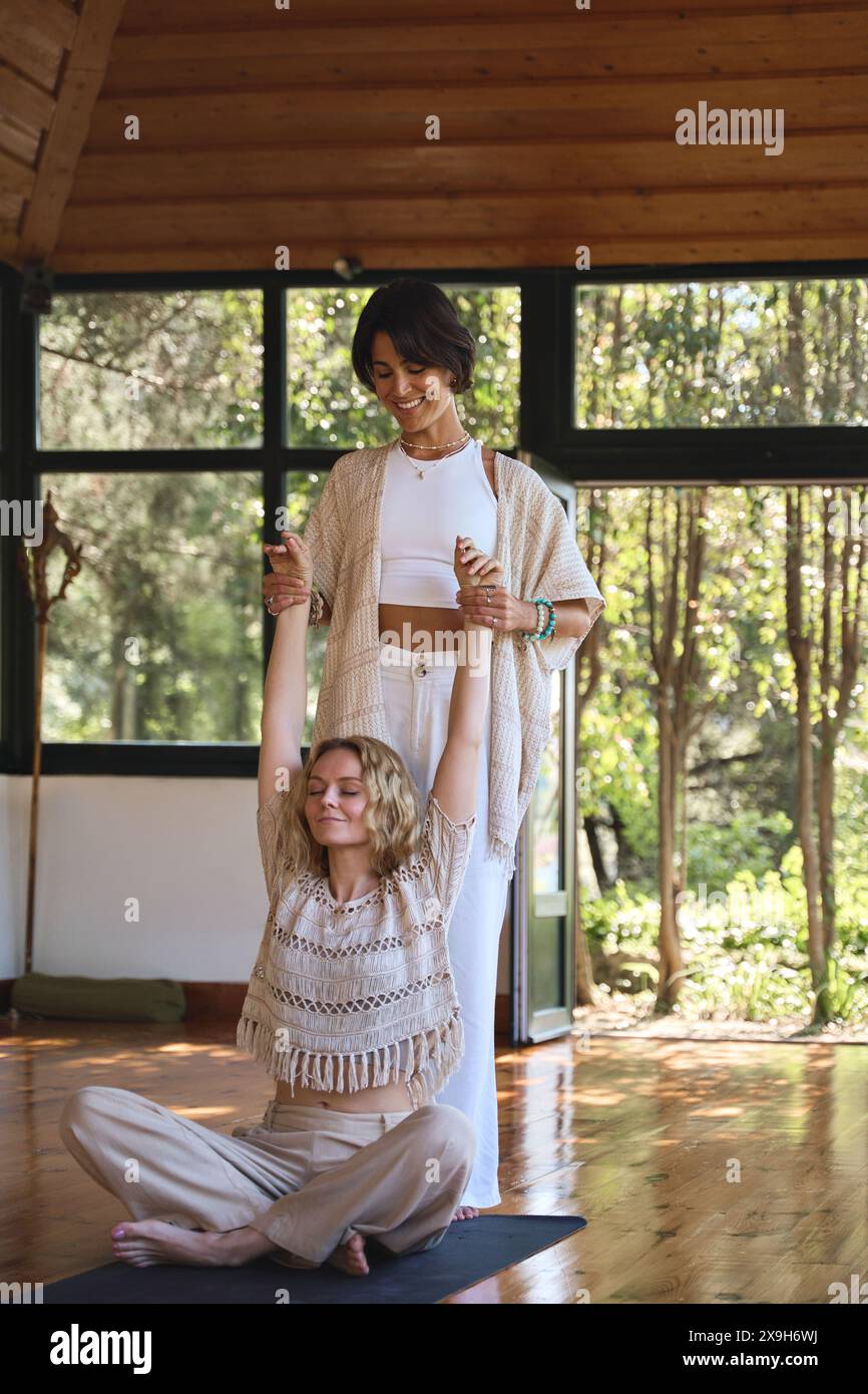 Happy female yoga teacher helping young woman teaching stretching ...