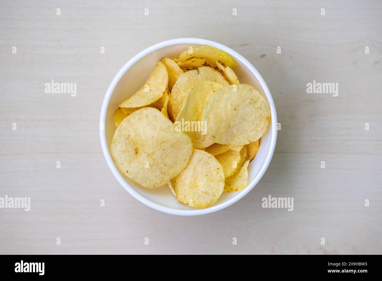 A bowl of crispy potato chips on a wooden background. Top view of ...