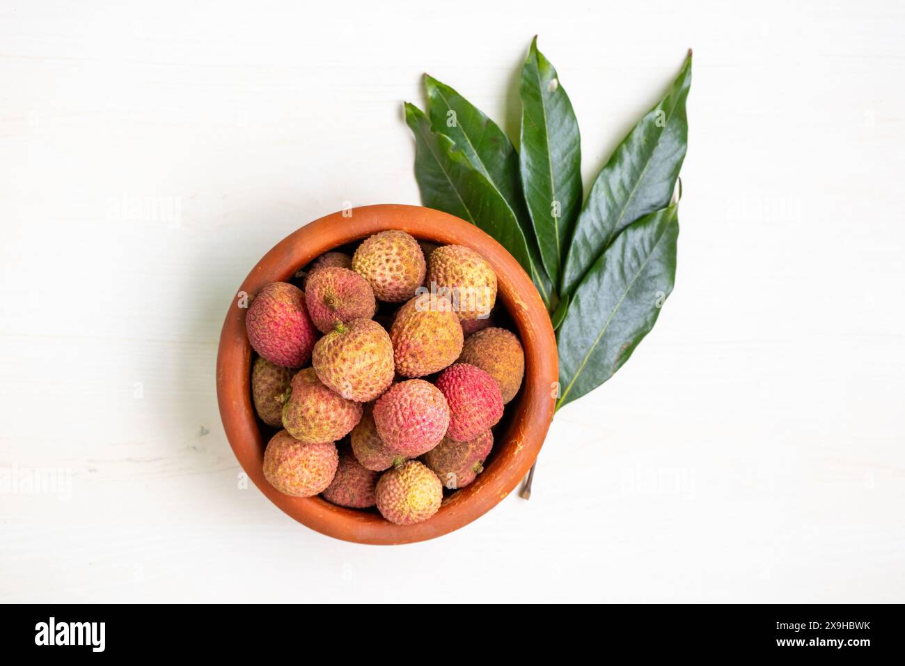 A bunch of fresh ripe lychee fruit on a clay pot with green leaves on a ...