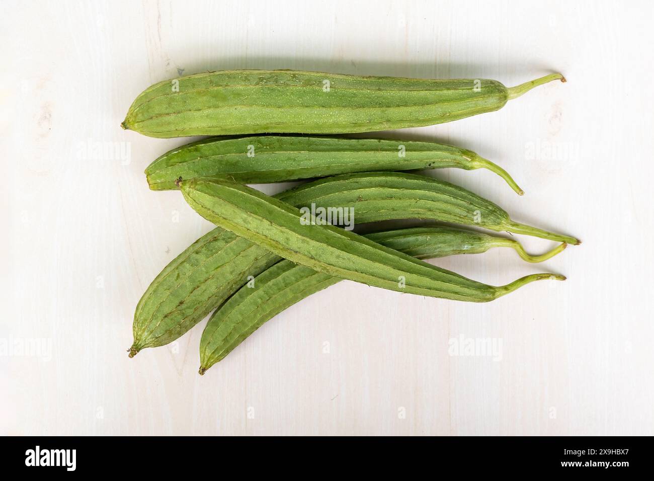 A bunch of fresh ridge gourds placed on a light wooden surface. It is ...