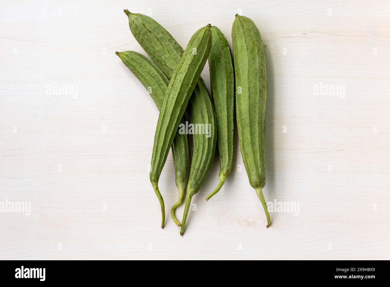A bunch of fresh ridge gourds placed on a light wooden surface. It is ...