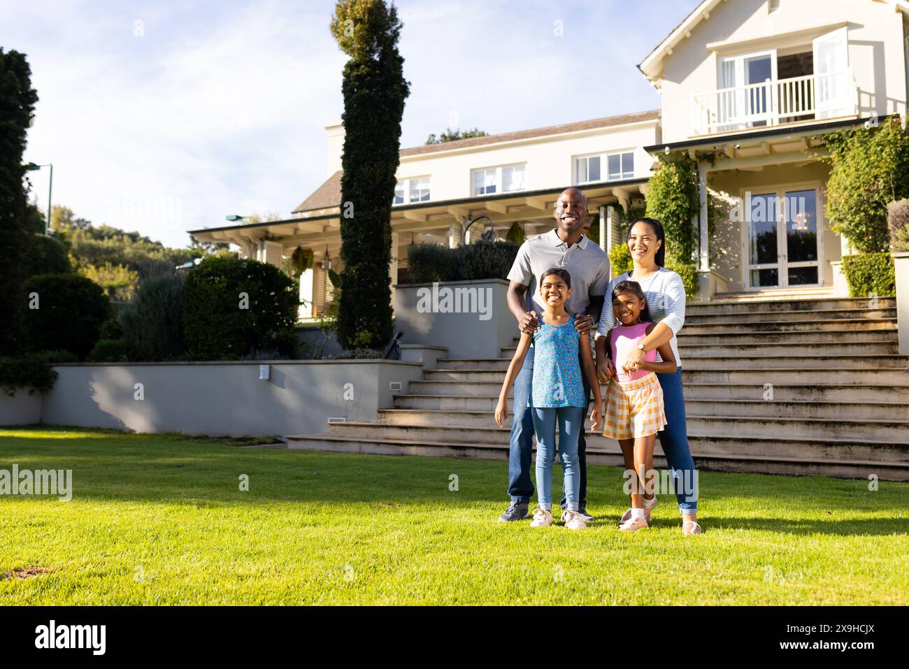 Outdoors, diverse family of four stands together smiling warmly by ...