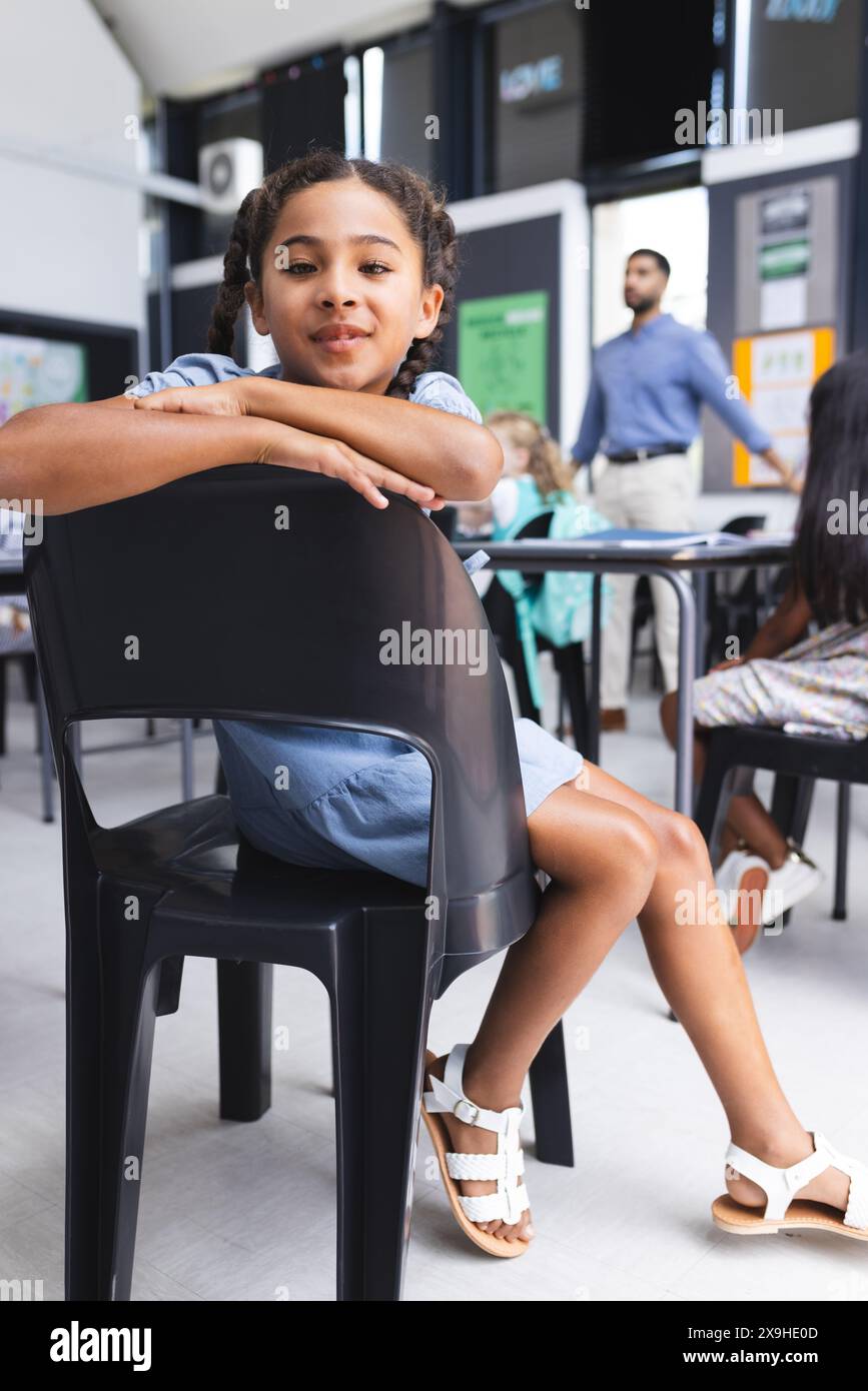 Biracial girl in a classroom sits casually on a chair, looking at the ...