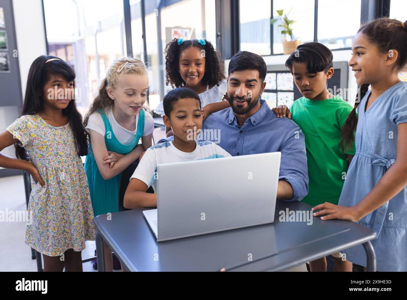 In school, young Asian male teacher and diverse students gather around ...