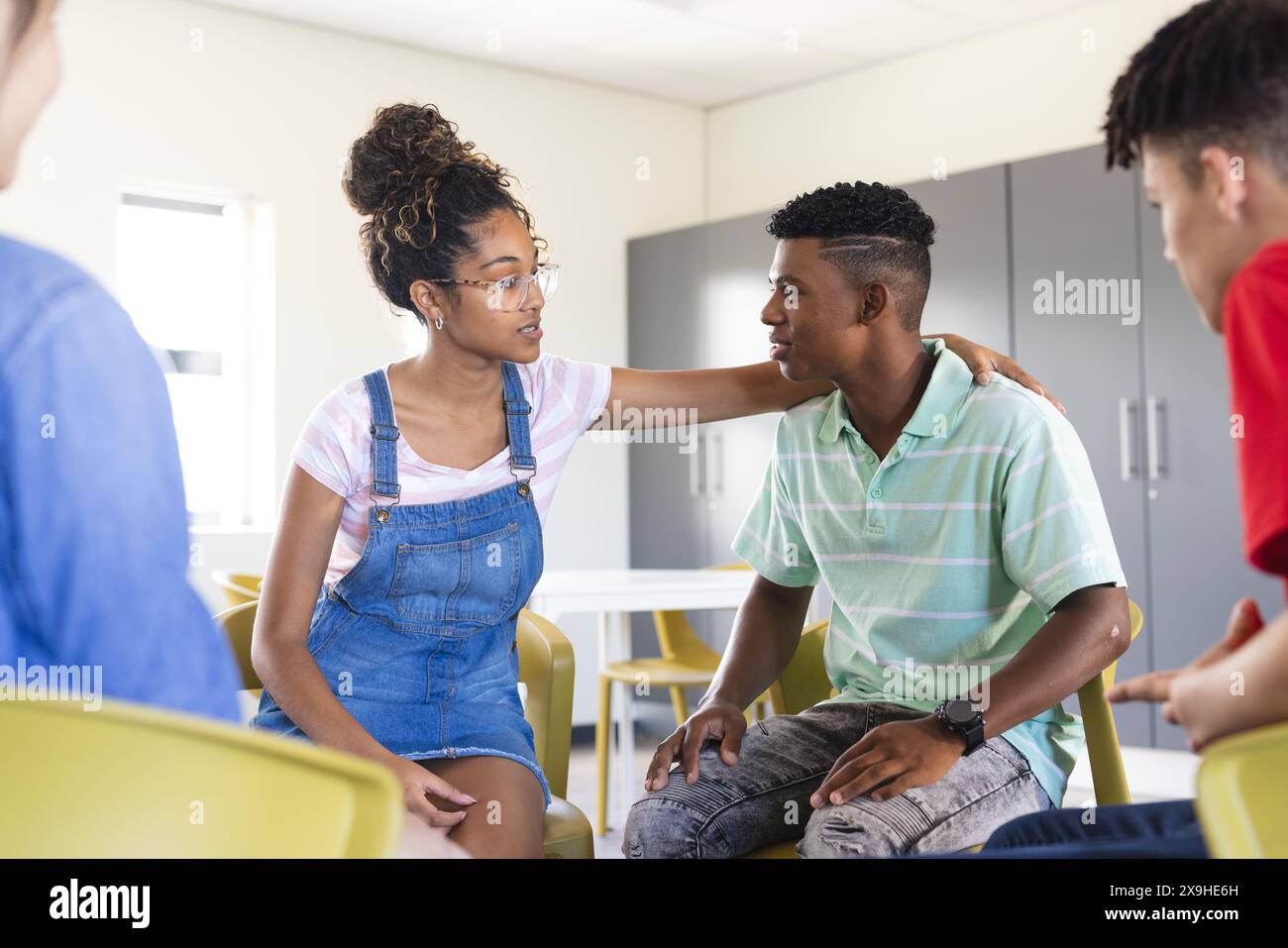 Teenage biracial boy comforts another in a high school setting. Group ...