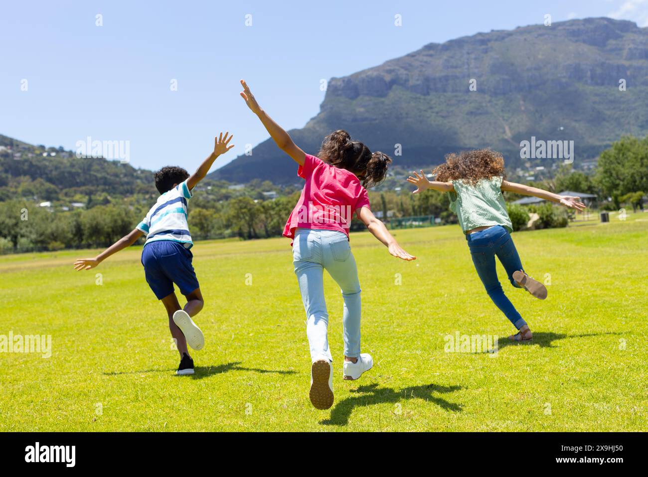 Three biracial children run joyfully across grassy field Stock Photo ...