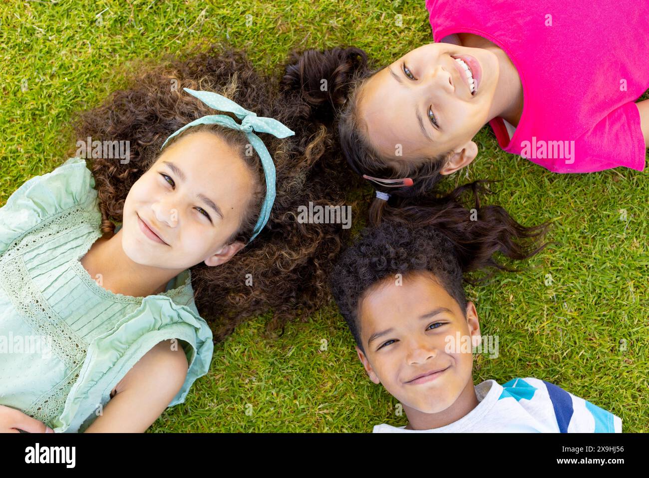 Three biracial children are lying on the grass, smiling up at the ...