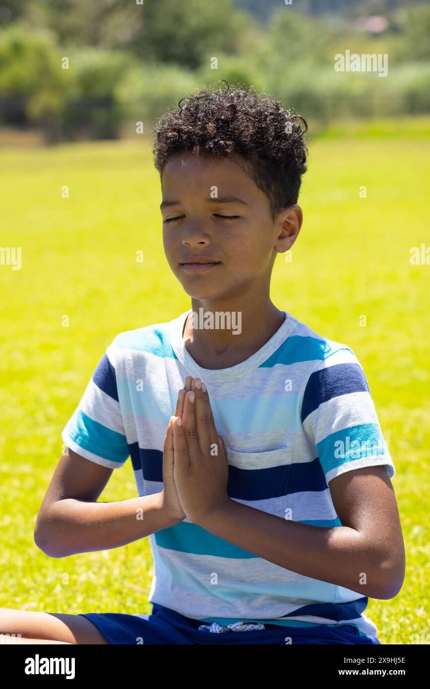 Biracial boy meditates with hands pressed together in a peaceful ...
