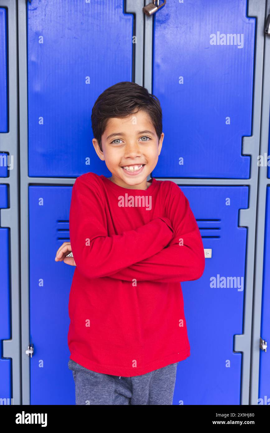 In school, young biracial male student leaning against blue lockers ...