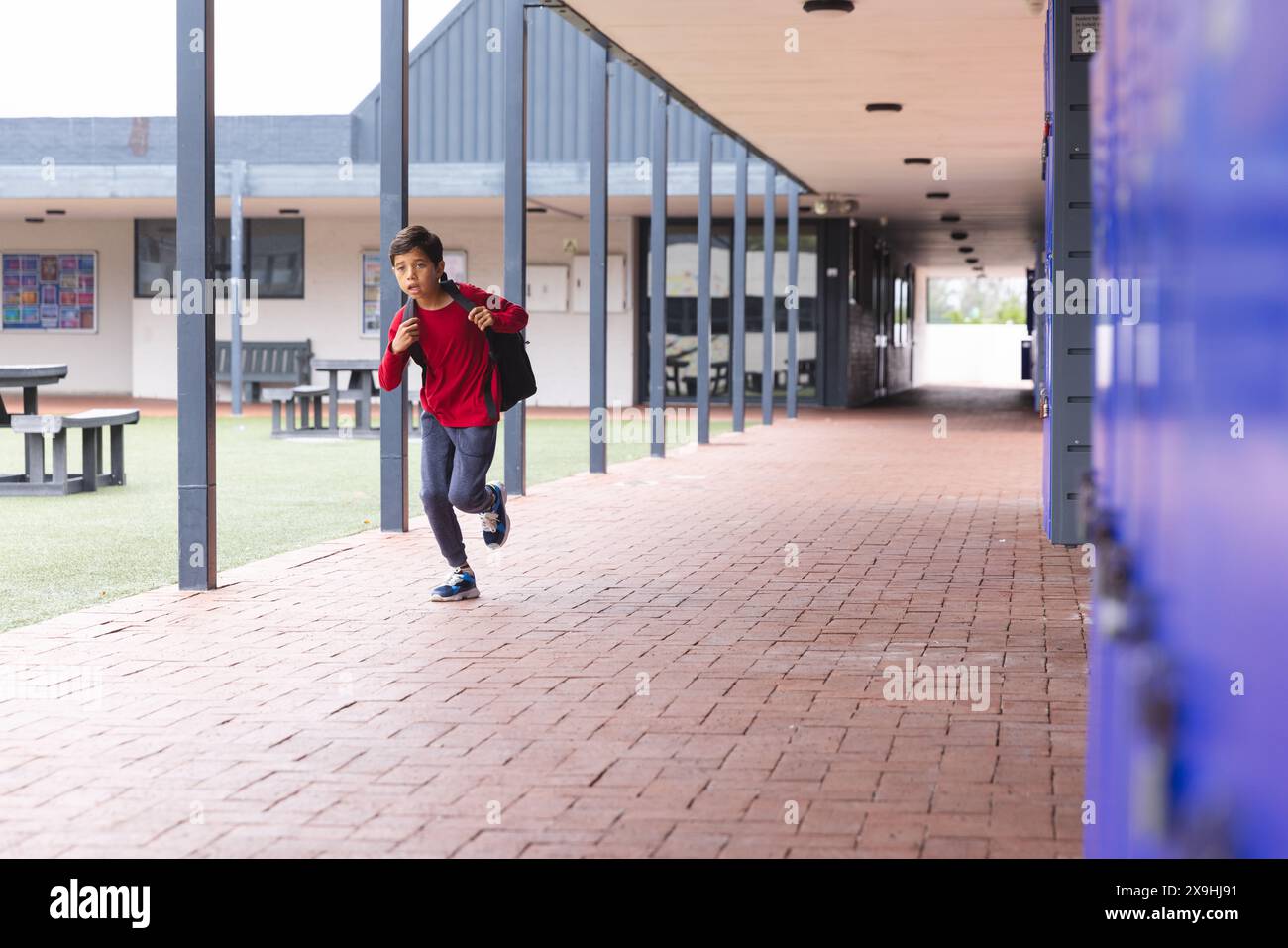 In school, outdoors, young biracial male student wearing a red backpack ...