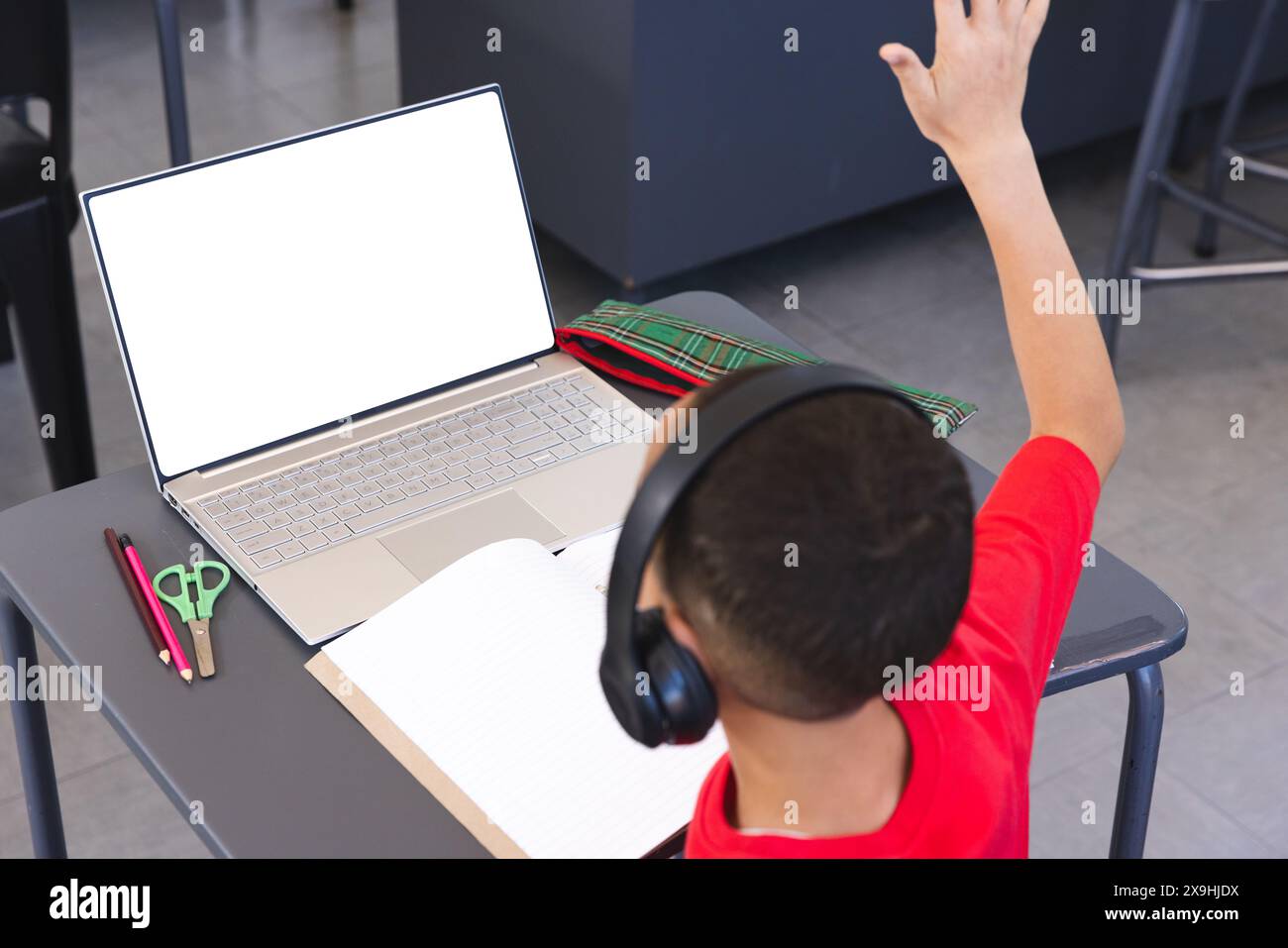 Biracial boy engaged in online learning at a school classroom using a ...