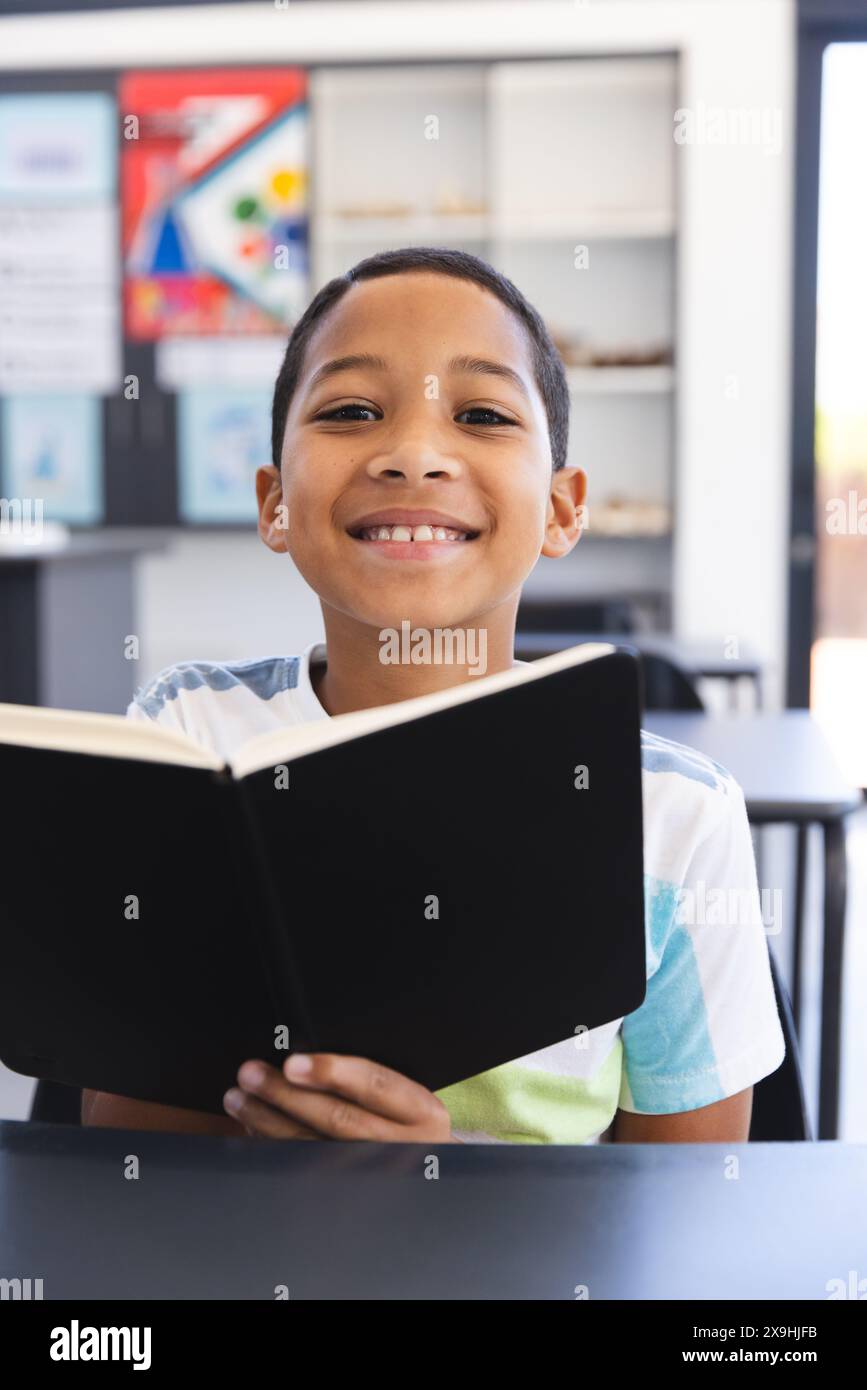 Biracial boy reading a book in a classroom at school, with copy space ...