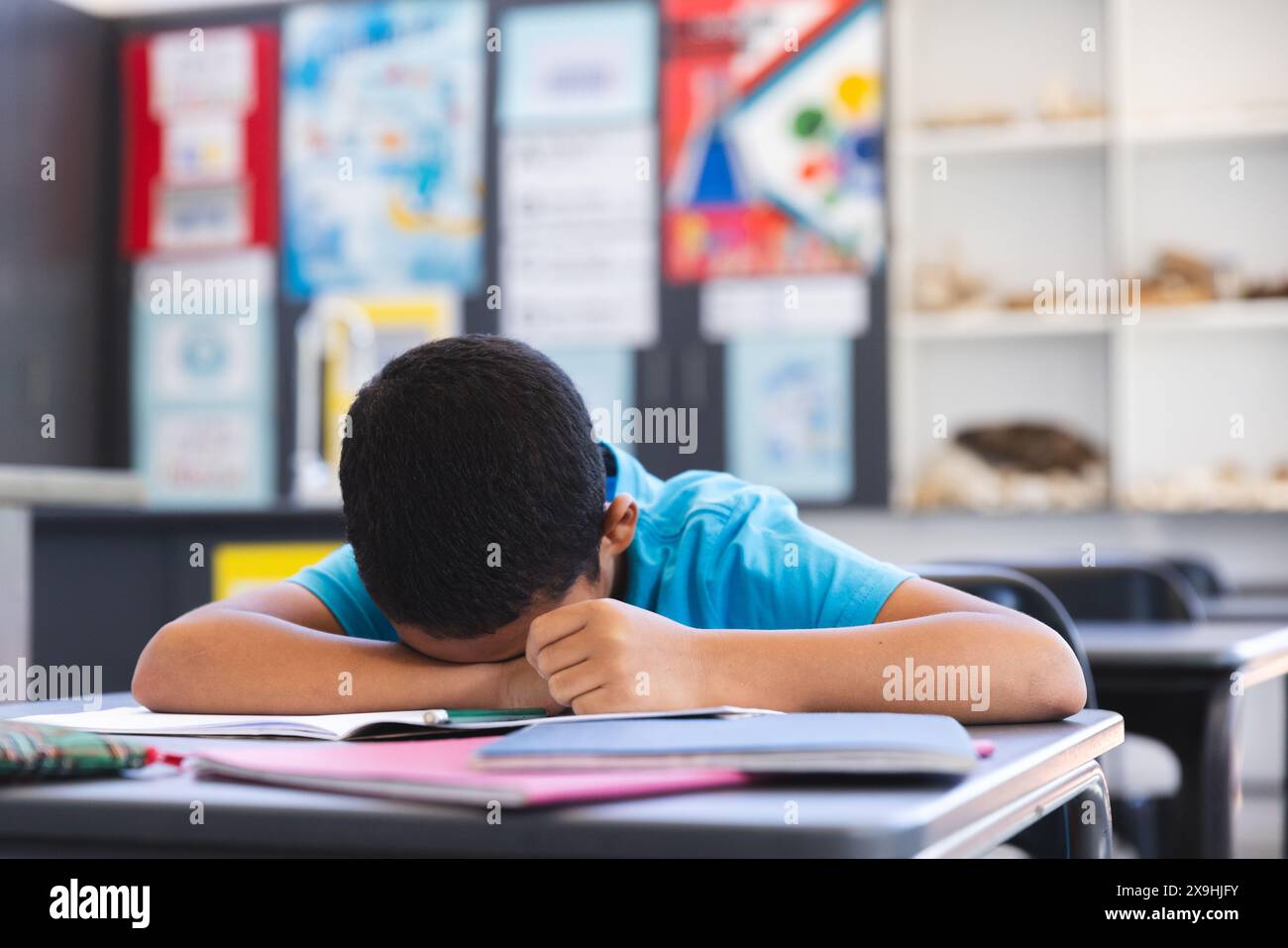 In a school classroom, a young Asian student rests his head on his arms ...