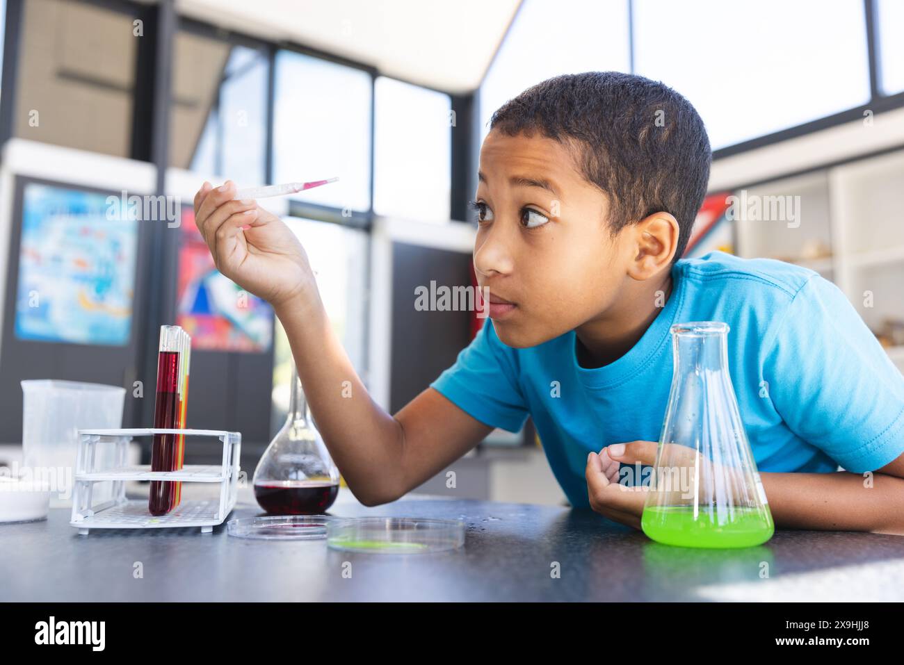 Biracial boy engaged in a science experiment at school in the classroom ...