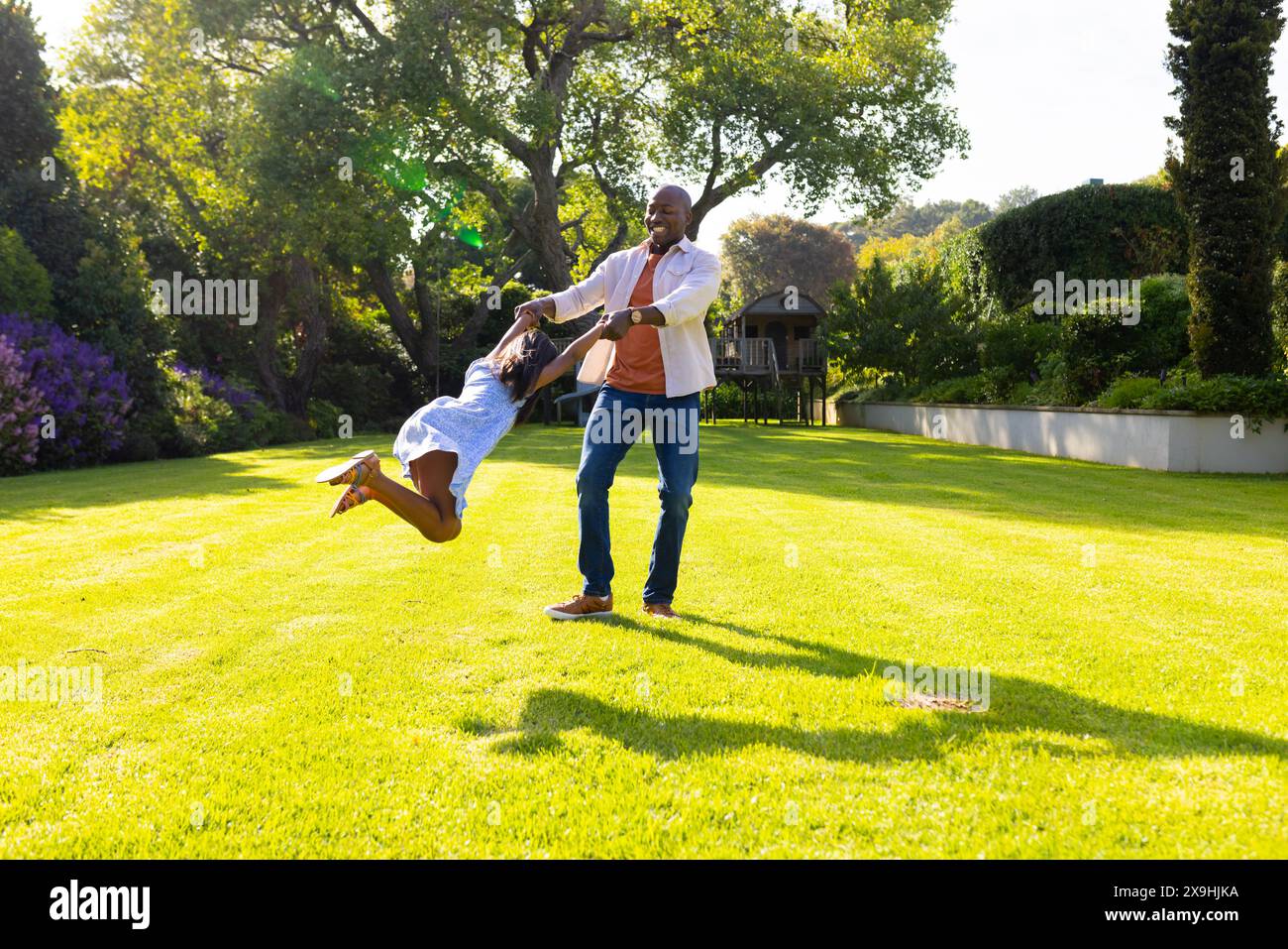Outdoors, diverse father and daughter swinging in sunny backyard Stock ...