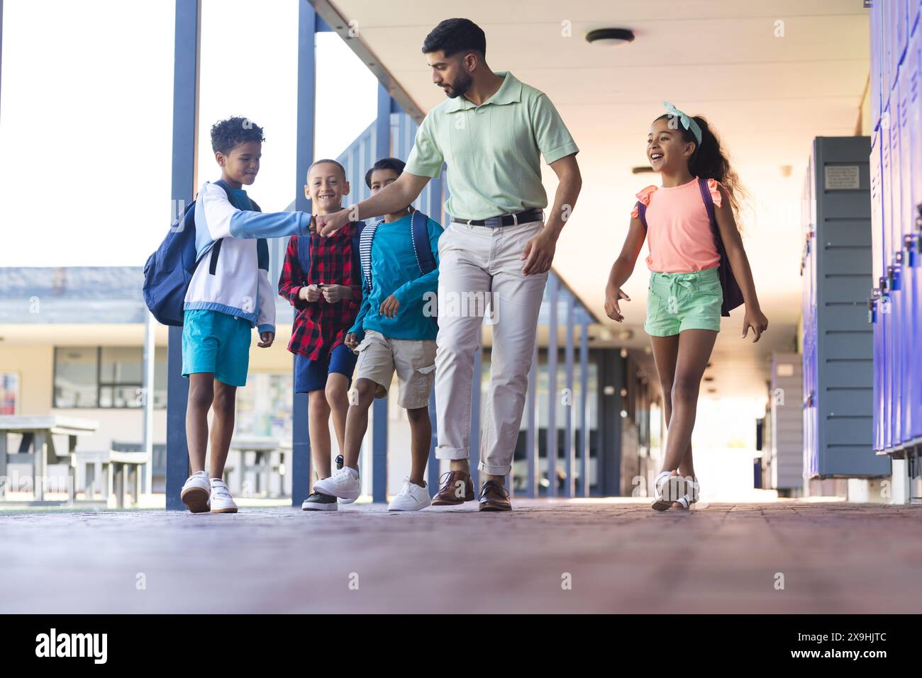 In school, Asian male teacher walks with three biracial boys and girl ...