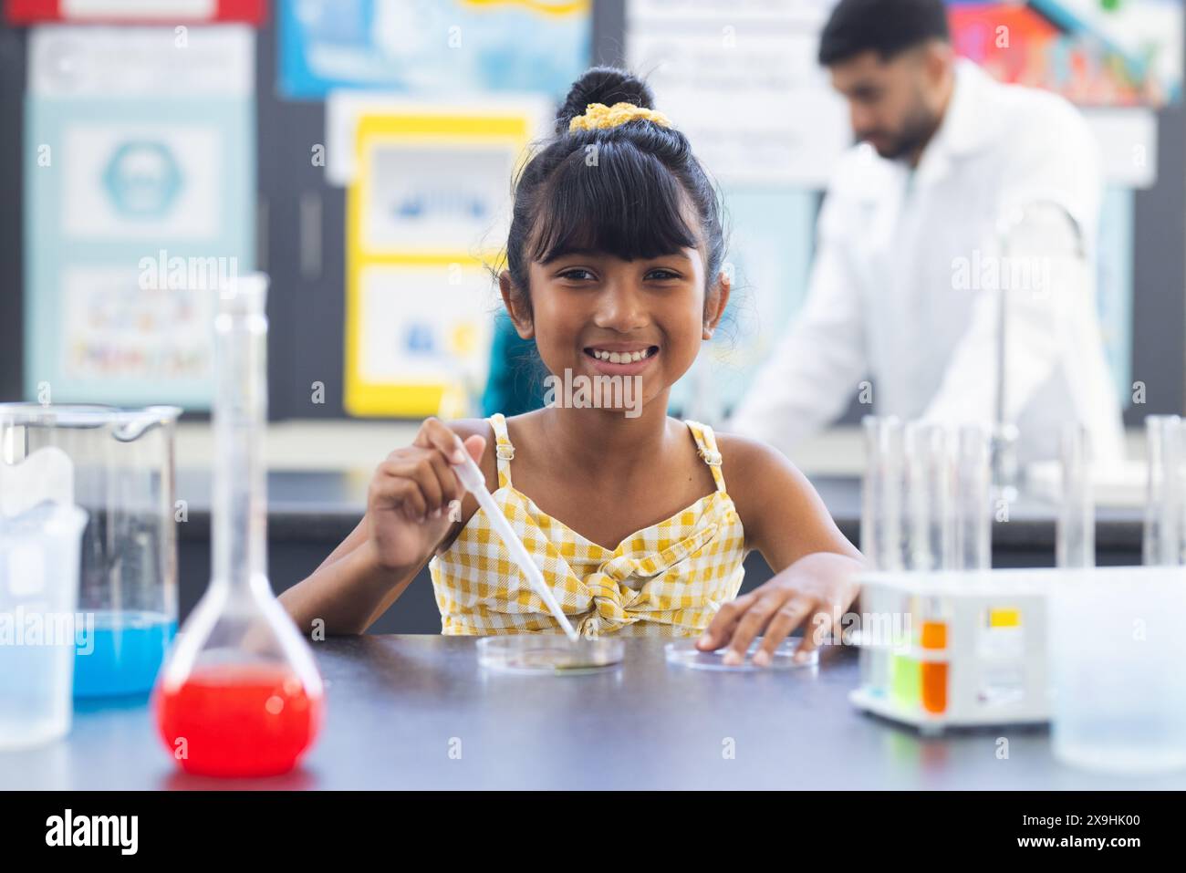 Biracial girl in yellow conducts experiment, male scientist watches ...