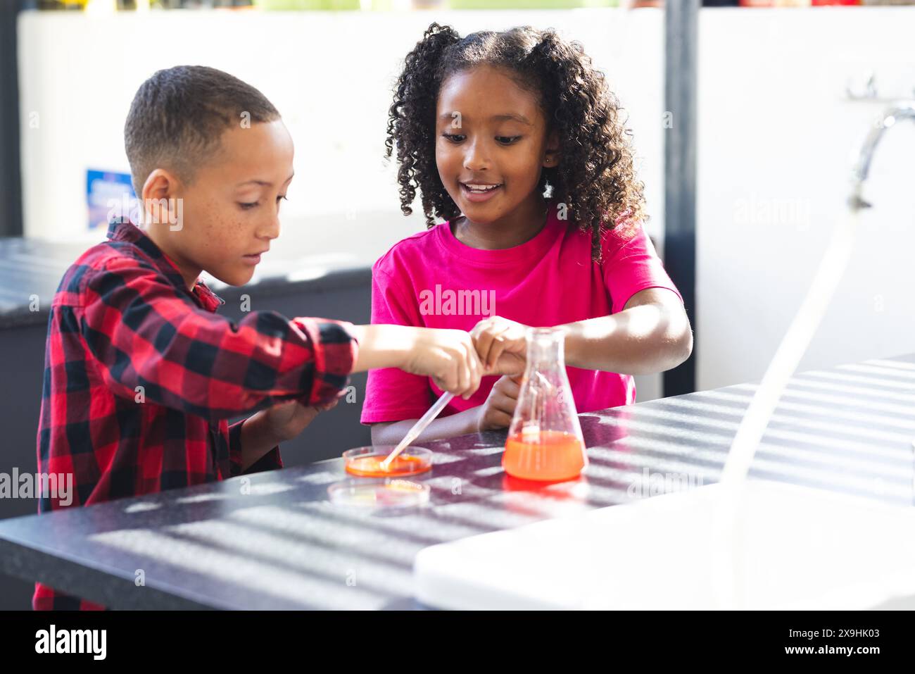 Biracial boy and girl engage in a science experiment in school, wearing ...
