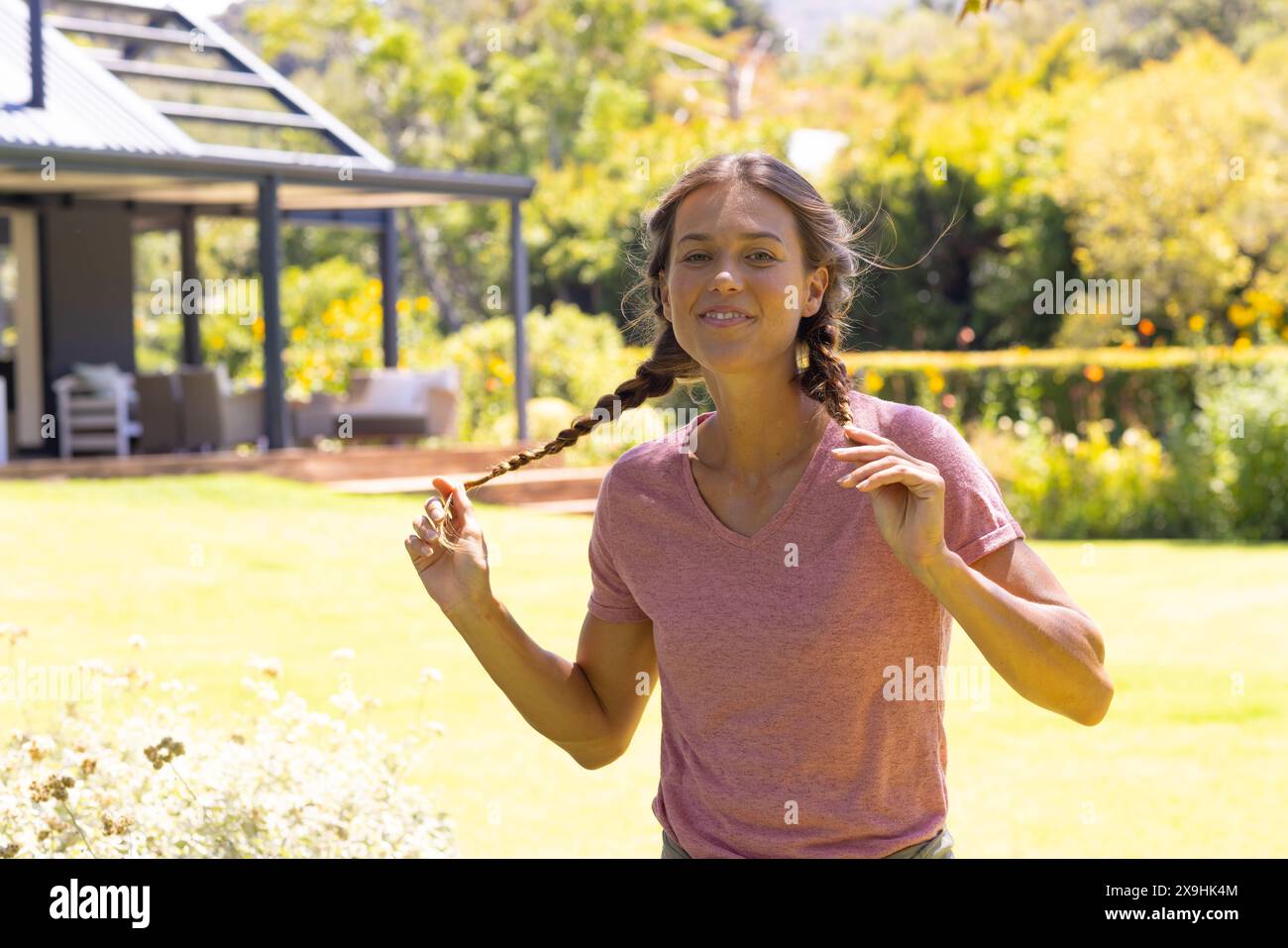 A caucasian young female holding her braid outside, wearing pink t ...