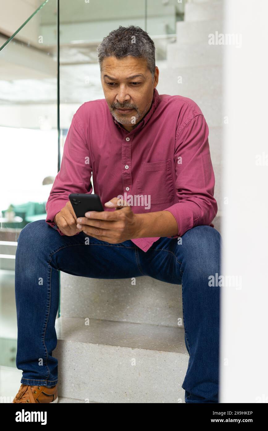 At home, biracial senior male with gray hair and beard sits on stairs ...