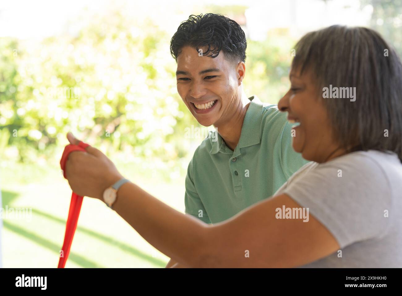 Young biracial male physiotherapist aids senior female patient at home ...